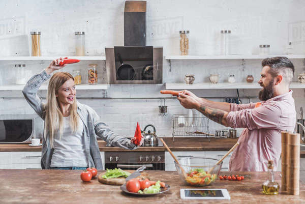 Funny couple playing with vegetables while cooking dinner at kitchen ...