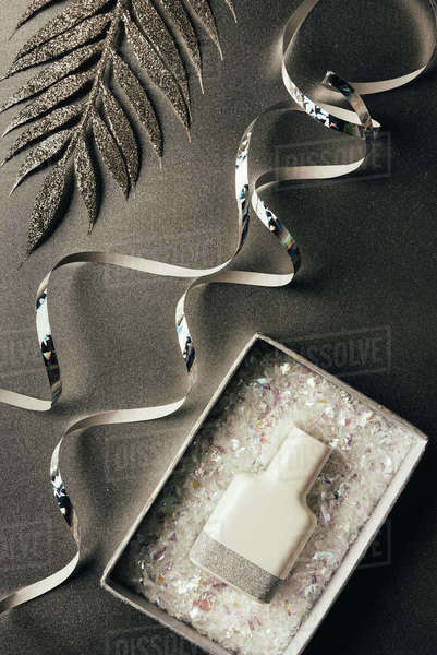 Perfume bottle in box, silver ribbons and shiny decorative leaves on ...