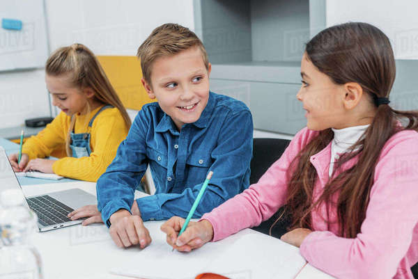 Smiling children sitting at desk and in modern classroom - Royalty-free ...