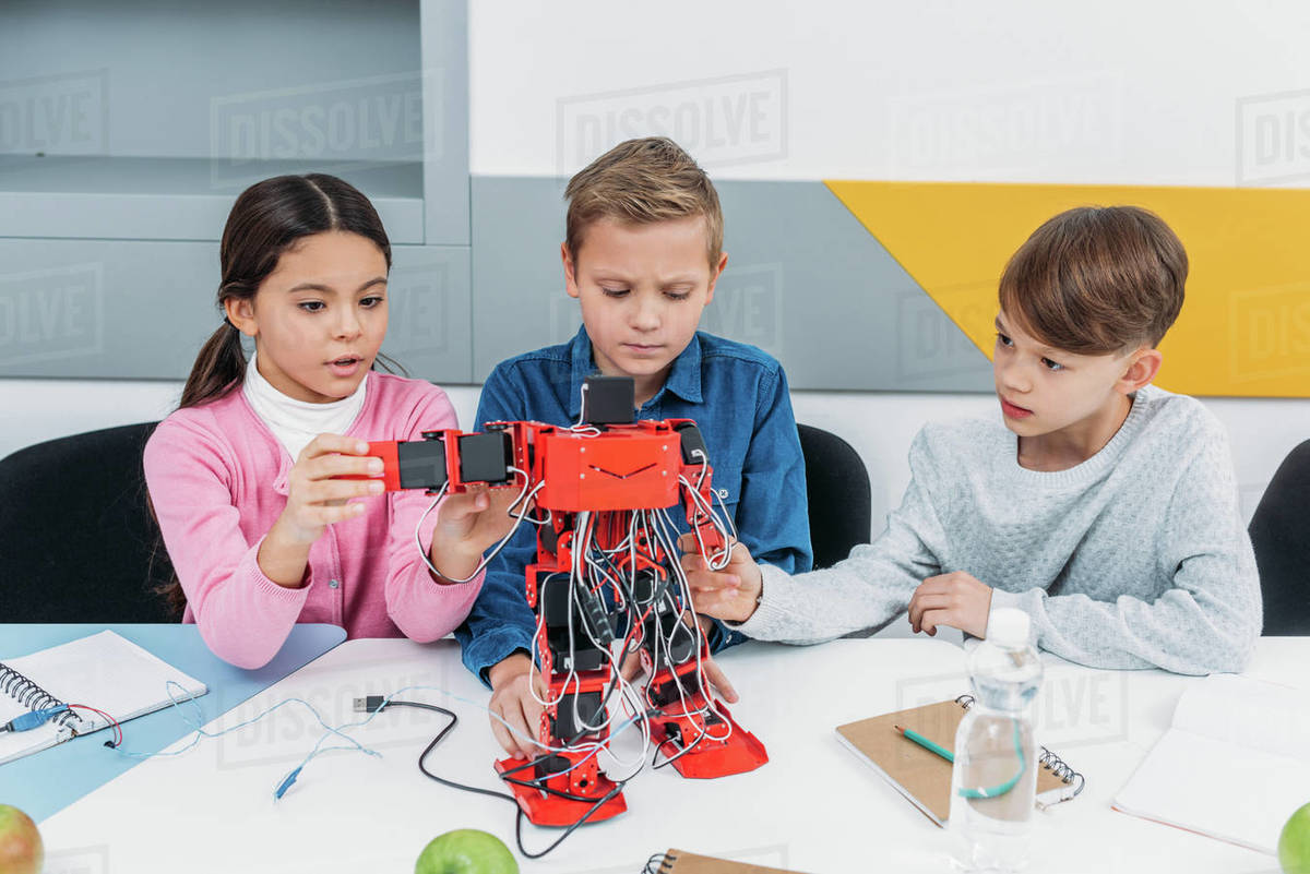 Concentrated schoolchildren constructing big red electric robot at desk ...