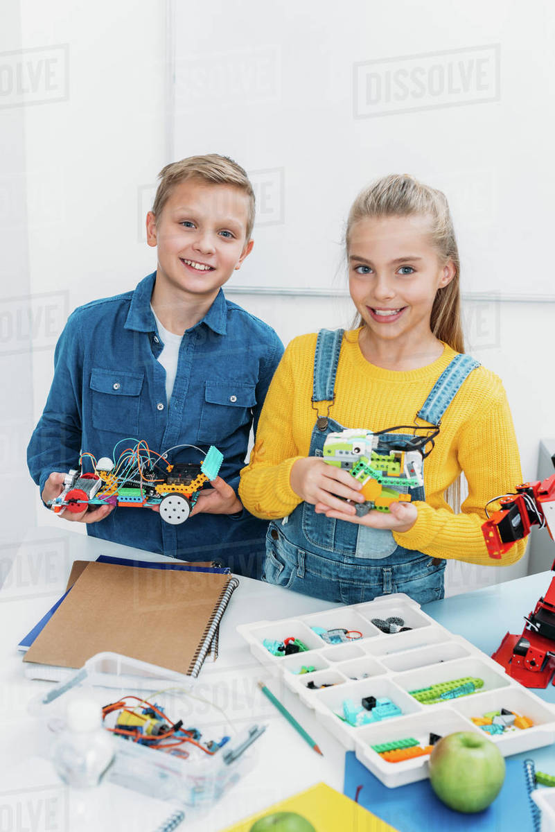 Smiling children holding electric robots in stem education class ...