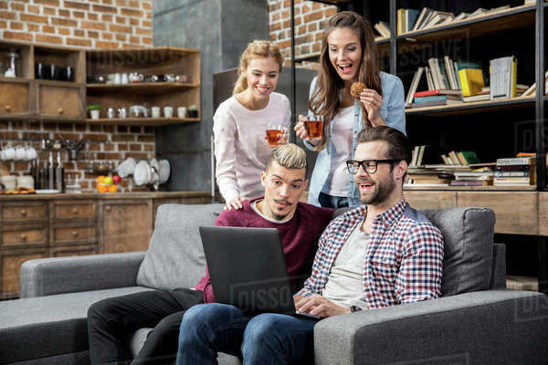 Happy friends using laptop and drinking tea in living room - Royalty ...