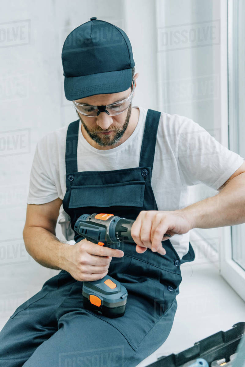 serious male handyman with electric drill sitting on windowsill - Stock ...