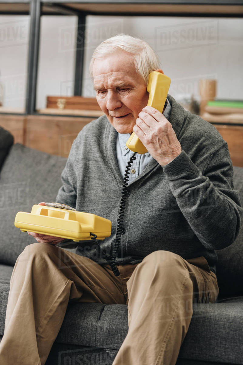 Retired man using old phone while sitting on sofa - Royalty-free Stock ...
