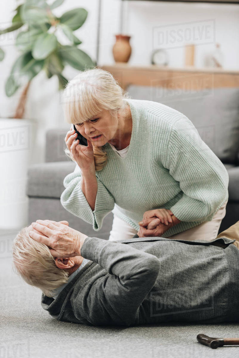 Senior woman helping to husband who fell down on floor and holding hand ...
