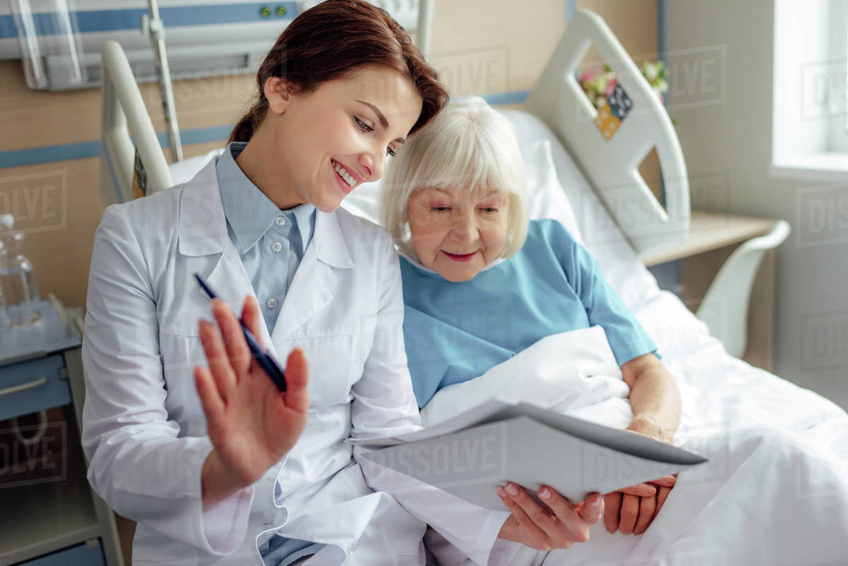 Happy female doctor holding diagnosis and consulting senior woman lying ...