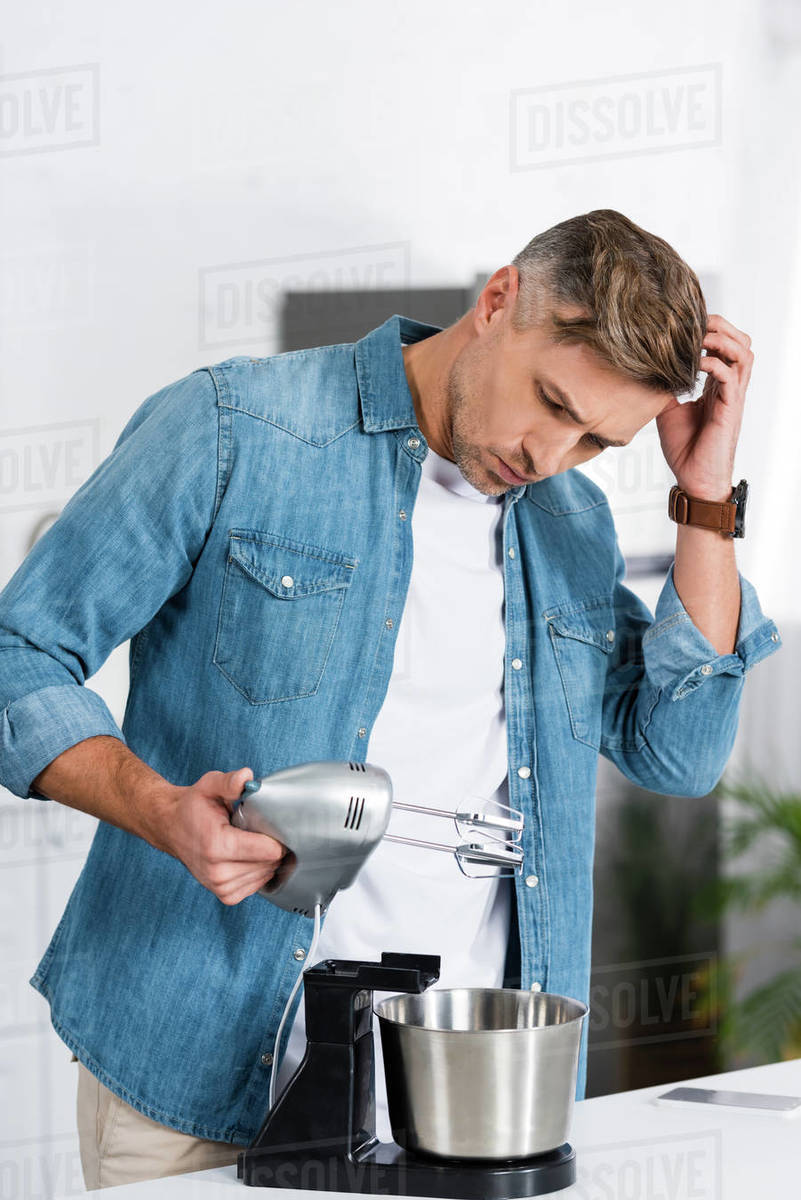 Confused handsome man holding kitchen mixer and scratching head ...