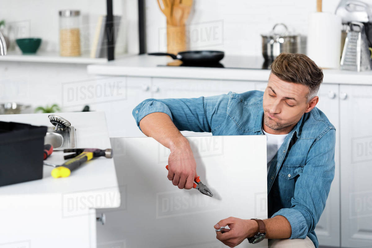 Sad man holding pliers in hand while repairing kitchen sink - Royalty ...