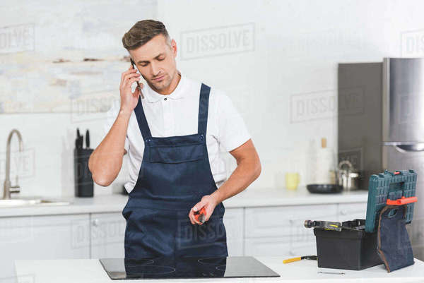 Adult repairman talking on smartphone and holding pliers while ...