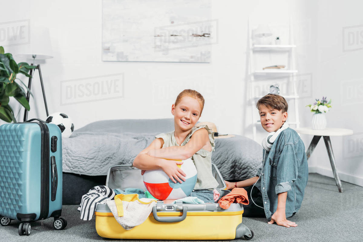 Happy kids packing clothes for trip while girls sitting in suitcase ...