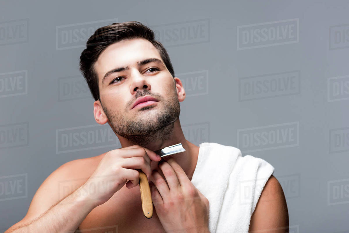 Young handsome man shaving with straight razor isolated on grey - Stock ...