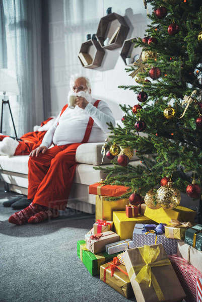 santa claus drinking coffee while sitting on sofa at home - Stock Photo ...