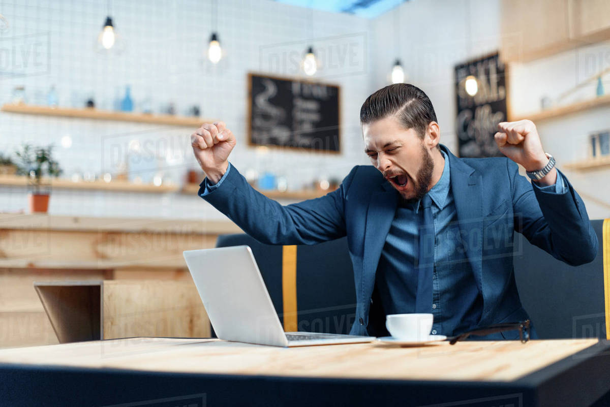 Excited young businessman triumphing while using laptop in cafe - Stock ...