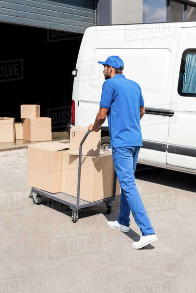 Delivery man driving cart with cardboard boxes into warehouse - Royalty ...