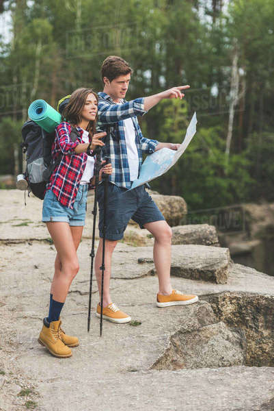 young couple of hikers with map on nature and pointing somewhere ...