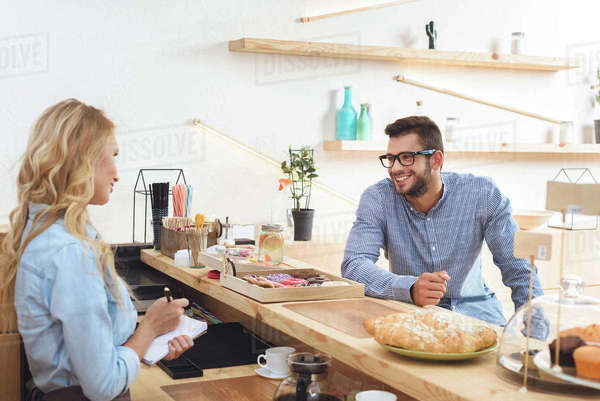 handsome young man in eyeglasses smiling and looking at waitress taking ...