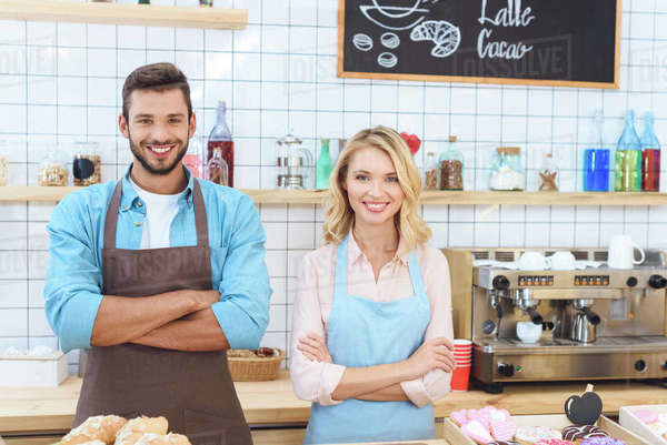 confident young cafe workers standing with crossed arms and smiling at ...