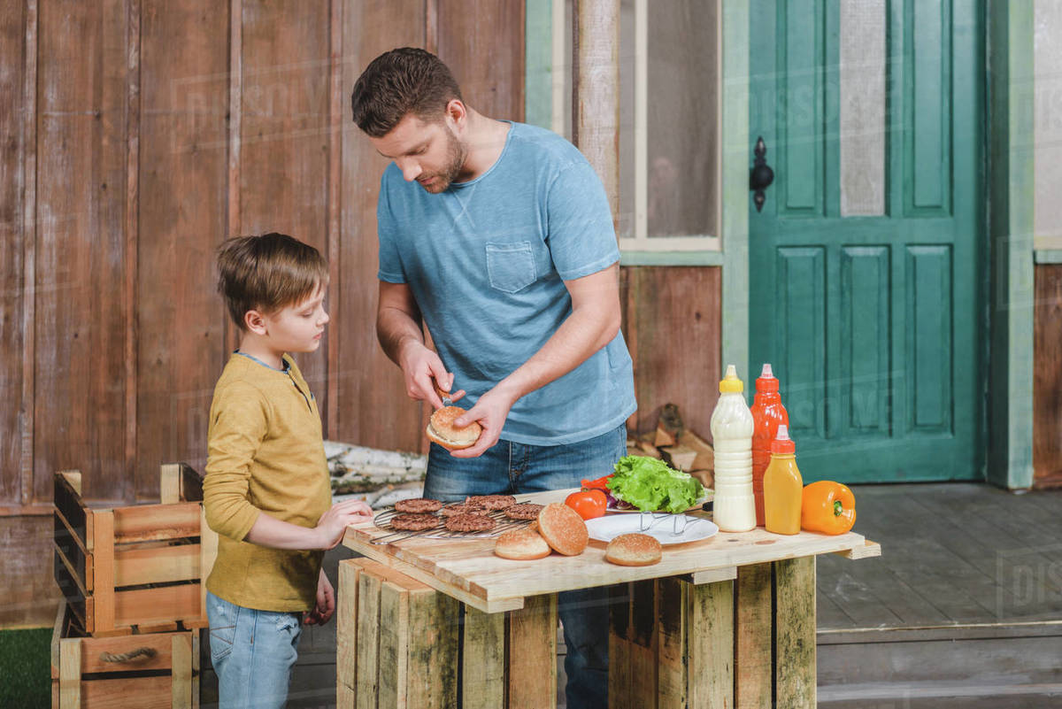 Side view of dad and son cooking meat burgers together - Stock Photo ...