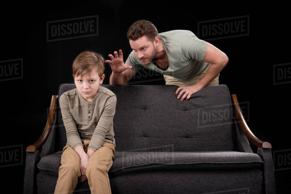 Angry father gesturing to scared little son sitting on sofa, family ...