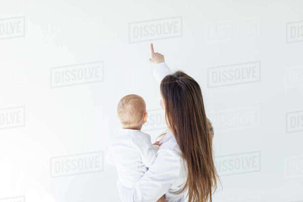 Rear view of mother holding adorable baby boy and pointing isolated on ...