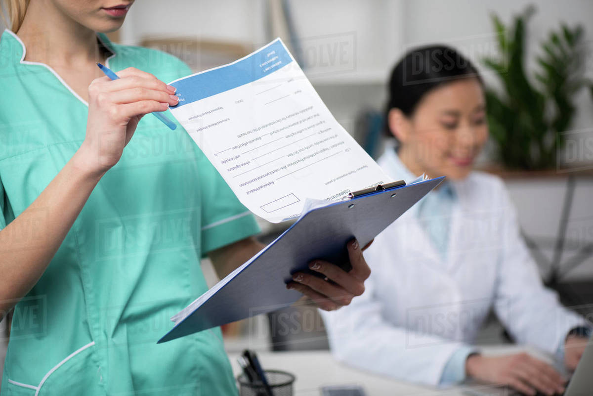 Partial view of doctor looking at clipboard with colleague behind ...