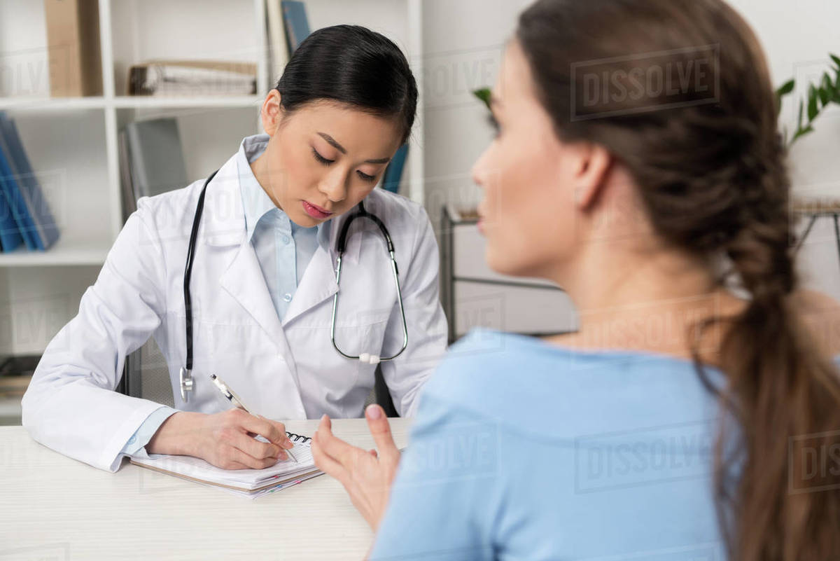 Doctor writing in notebook while patient telling about illness at ...