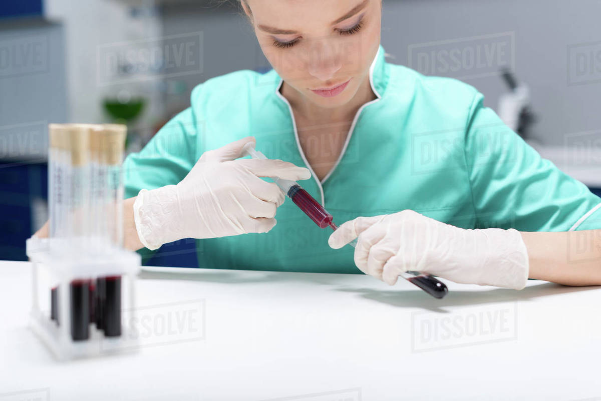 Nurse pouring blood samples from syringe into tubes at laboratory ...