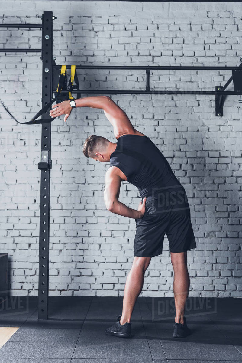 Back view of young man in sportswear stretching before training in gym ...