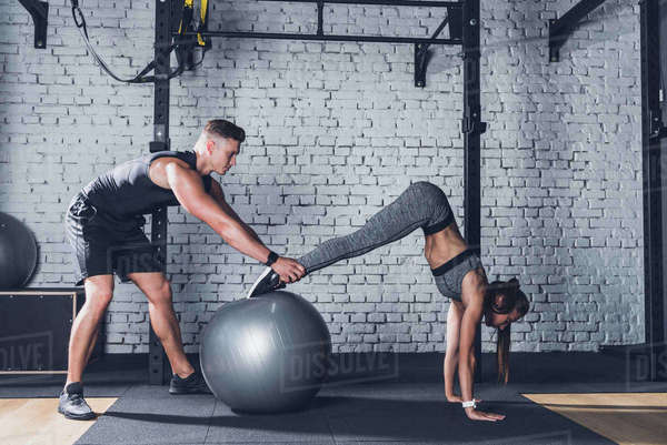 Side view of trainer holding sportive woman while she working out on ...
