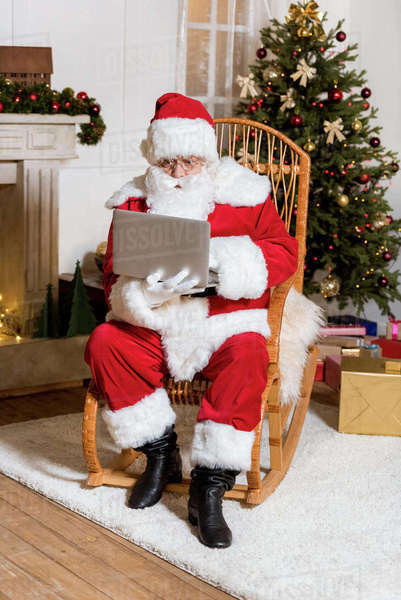 Santa Claus resting in rocking chair and typing on laptop at home ...