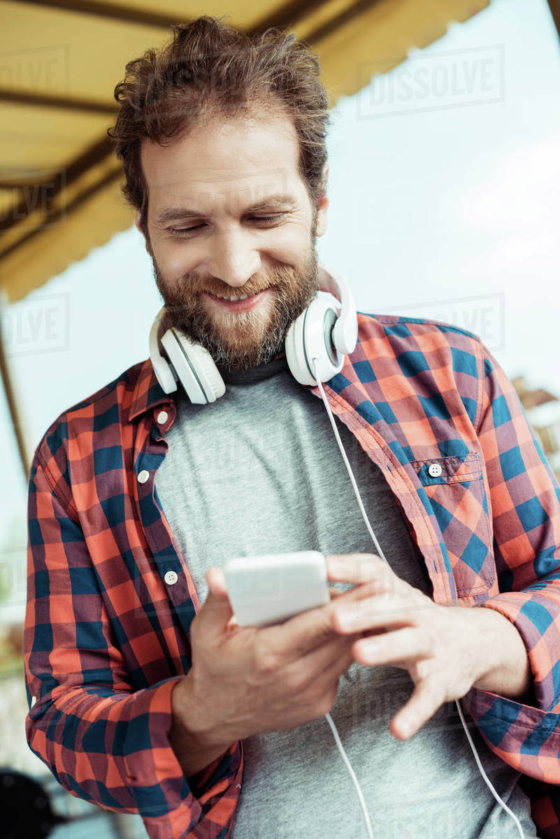 Portrait of smiling man with headphones hanging on neck using ...