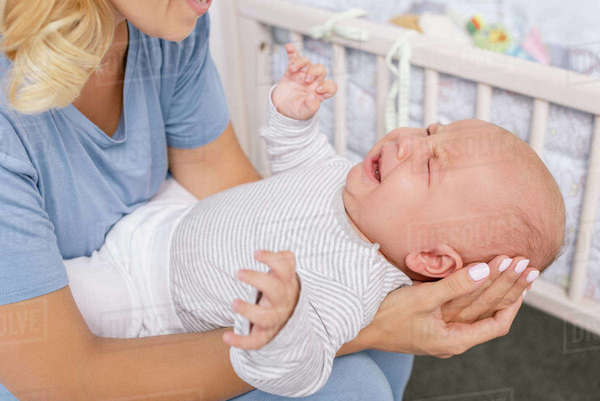 Cropped shot of mother holding crying baby in hands at home - Stock ...