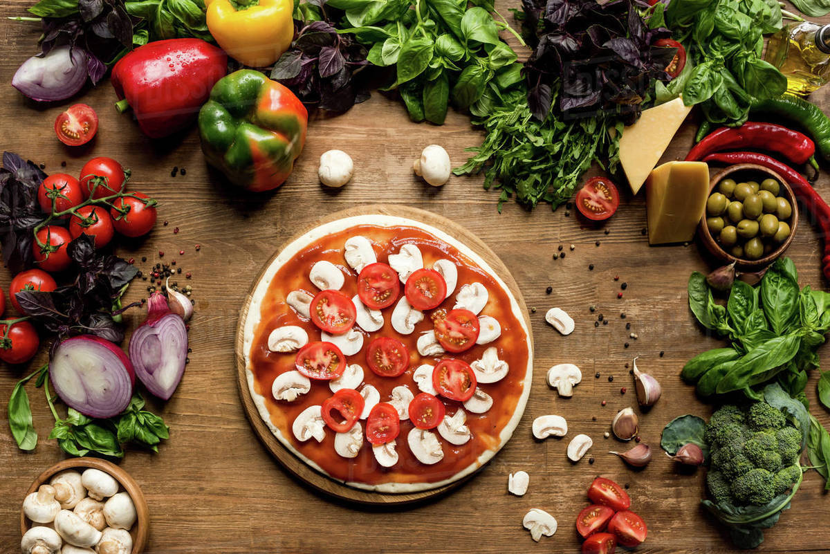 Top view of raw homemade pizza and fresh ingredients on wooden tabletop ...