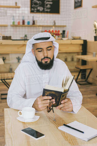 young muslim man reading quran sitting in modern cafe - Stock Photo ...