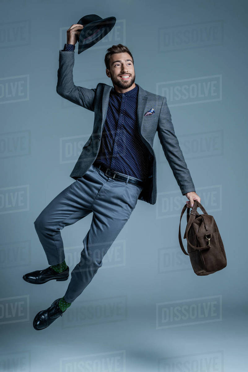 Smiling young man in suit jumping up and raising his hat - Stock Photo ...
