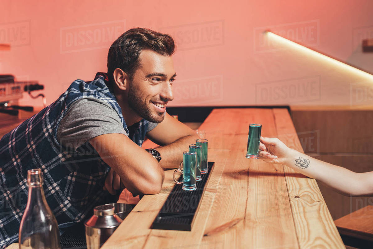 Side view of smiling barman looking a visitor at counter in bar ...