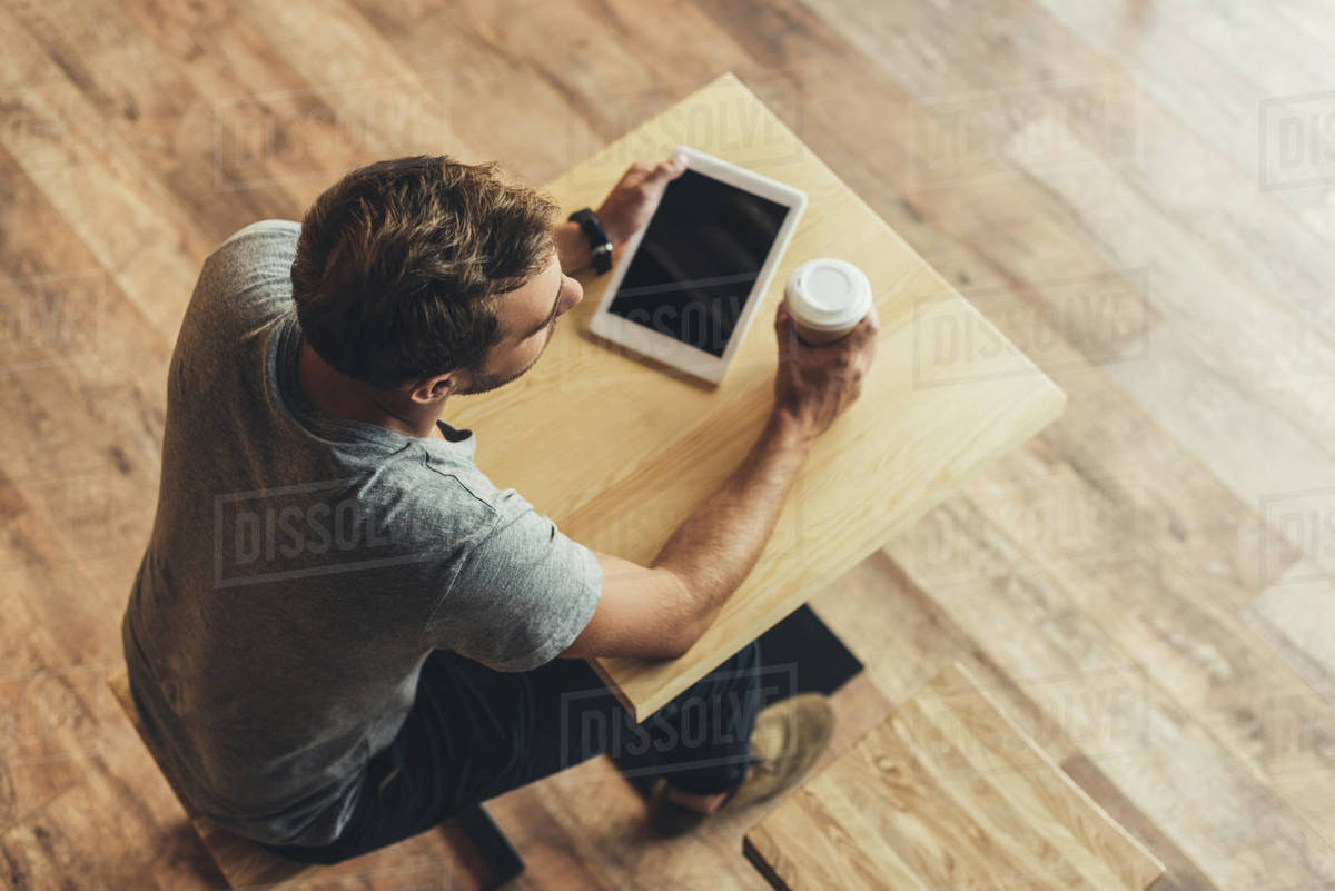 Overhead view of man sitting at table with coffee to go and tablet in ...