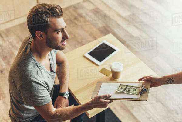 Side view of young man paying for order with cash in cafe - Stock Photo ...