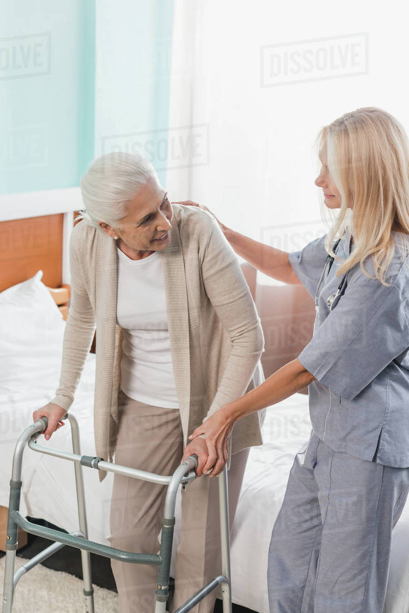 nurse and senior patient with walker smiling each other in hospital ...