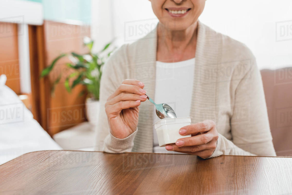 cropped shot of smiling senior woman eating yogurt in hospital ...