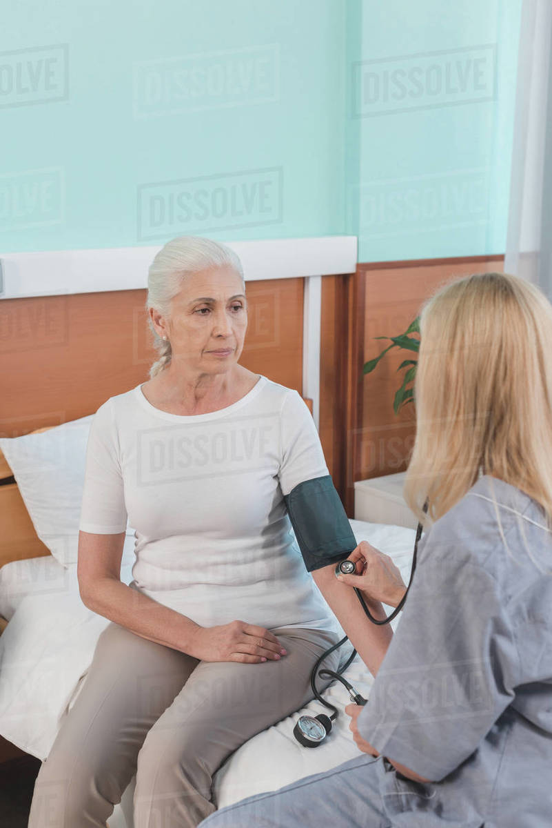 nurse measuring blood pressure to senior woman in hospital - Royalty ...