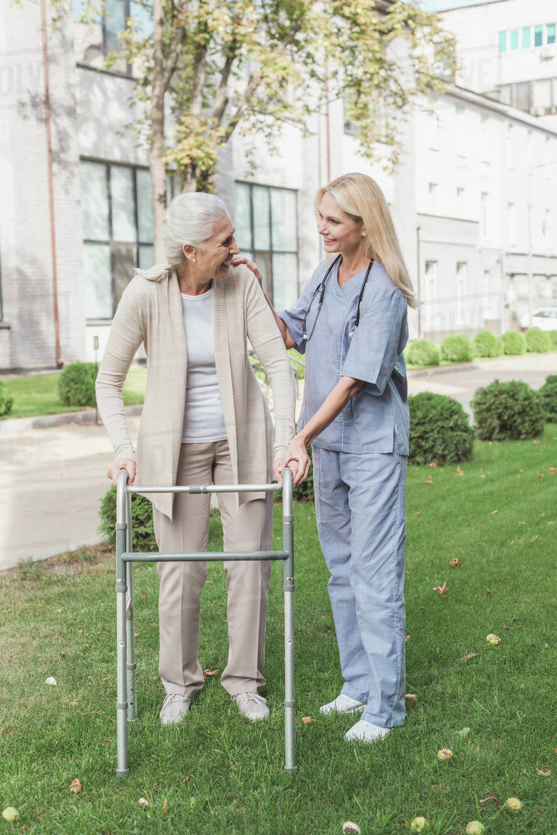 nurse and senior patient with walker smiling each other outside nursing ...