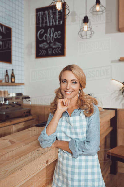 attractive cheerful cafe owner in apron smiling at camera - Stock Photo ...