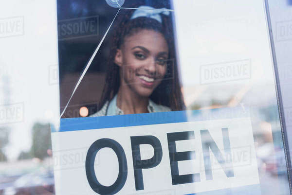 Young African American woman hanging an open sign on a glass door ...