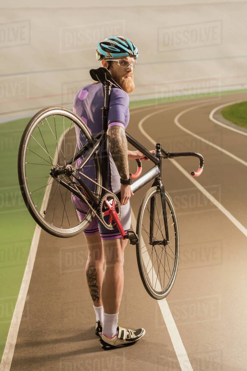 Back view of cyclist with bicycle in hands looking at camera while ...