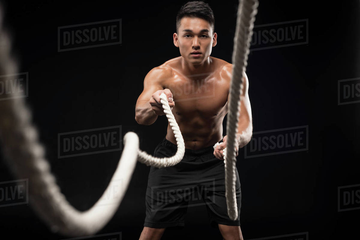 Muscular shirtless young man doing battle ropes exercise isolated on ...