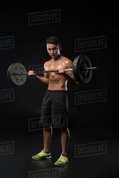 Full length view of shirtless muscular man lifting barbell and looking ...