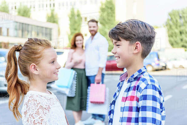Smiling sister and brother looking at each other while parents with ...
