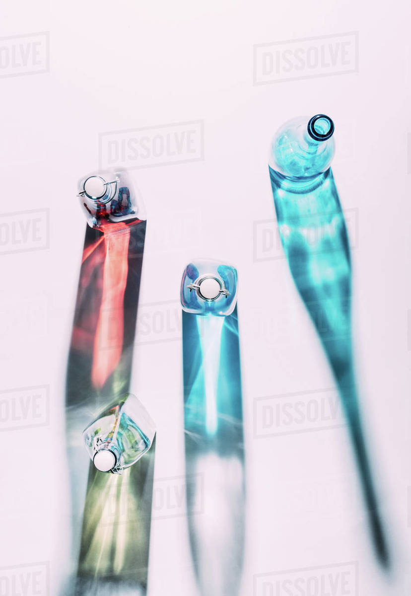 Top view shot of colorful glass bottles casting rainbow shadows on baby-pink tabletop - Stock ...