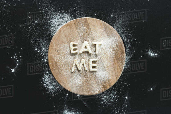 Top view of edible lettering eat me from dough on wooden cutting board ...